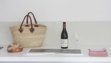 Uma cesta de vime, uma garrafa de vinho, uma taça de vinho, um pão e um livro sobre uma superfície branca.