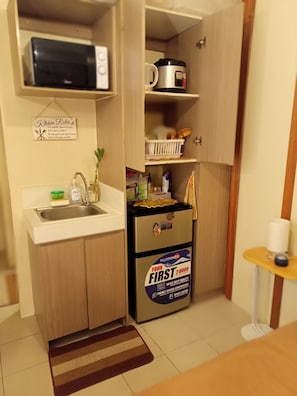 Cozinha compacta com pia, micro-ondas, geladeira e uma pequena mesa com uma xícara.