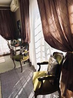 Um quarto com janela, uma cadeira, uma mesa e cortinas.