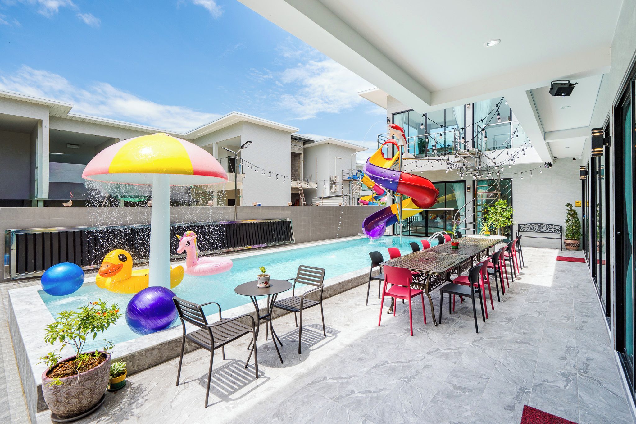 Uma área de piscina moderna ao ar livre, com escorregador, espreguiçadeiras e mesa de jantar.