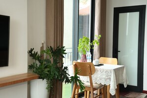Uma sala de jantar com uma mesa posta para dois, uma cadeira, um vaso de planta e uma janela com cortinas.