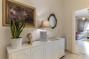 Um aparador branco com um vaso de planta, um quadro emoldurado, um abajur e um espelho.
