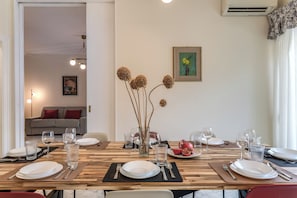 Uma área de refeições com mesa de madeira posta para uma refeição, um vaso com flores secas e um quadro na parede.