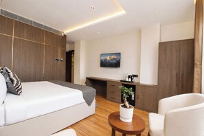 Quarto de hotel moderno com cama, escrivaninha, cadeira, cafeteira e planta em vaso.