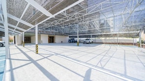 Amplo espaço de estacionamento coberto, com teto alto e estrutura metálica.
