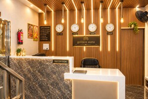 Bancada de recepção com tampo de mármore, relógios exibindo diferentes fusos horários e placa indicando as instalações do hotel 'golden aura'.