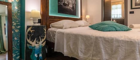 Quarto com cama, mesa de cabeceira, luminária na parede e quadro emoldurado sobre a cama.