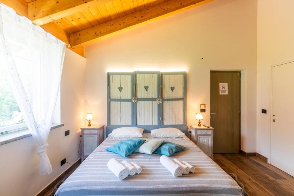 Quarto de hotel com cama, luminárias de cabeceira, porta e janela com cortinas.
