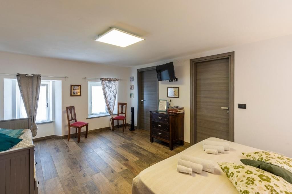Quarto com cama, cômoda, cadeira, escrivaninha, televisão e porta.