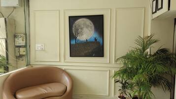 Uma sala de estar com uma obra de arte emoldurada representando uma árvore e veados sob uma lua cheia, um sofá de couro marrom e uma planta em vaso.