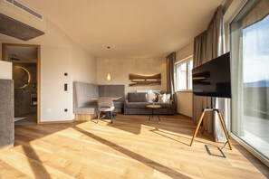 Uma sala de estar moderna com piso de madeira, um sofá, uma poltrona, uma TV sobre um móvel e uma janela grande.