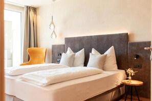 Quarto de hotel com uma cama grande, uma cadeira, uma mesa pequena e uma janela com cortinas.