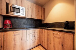 Cozinha com armários de madeira, micro-ondas de aço inoxidável, cafeteira vermelha e máquina de café preta.