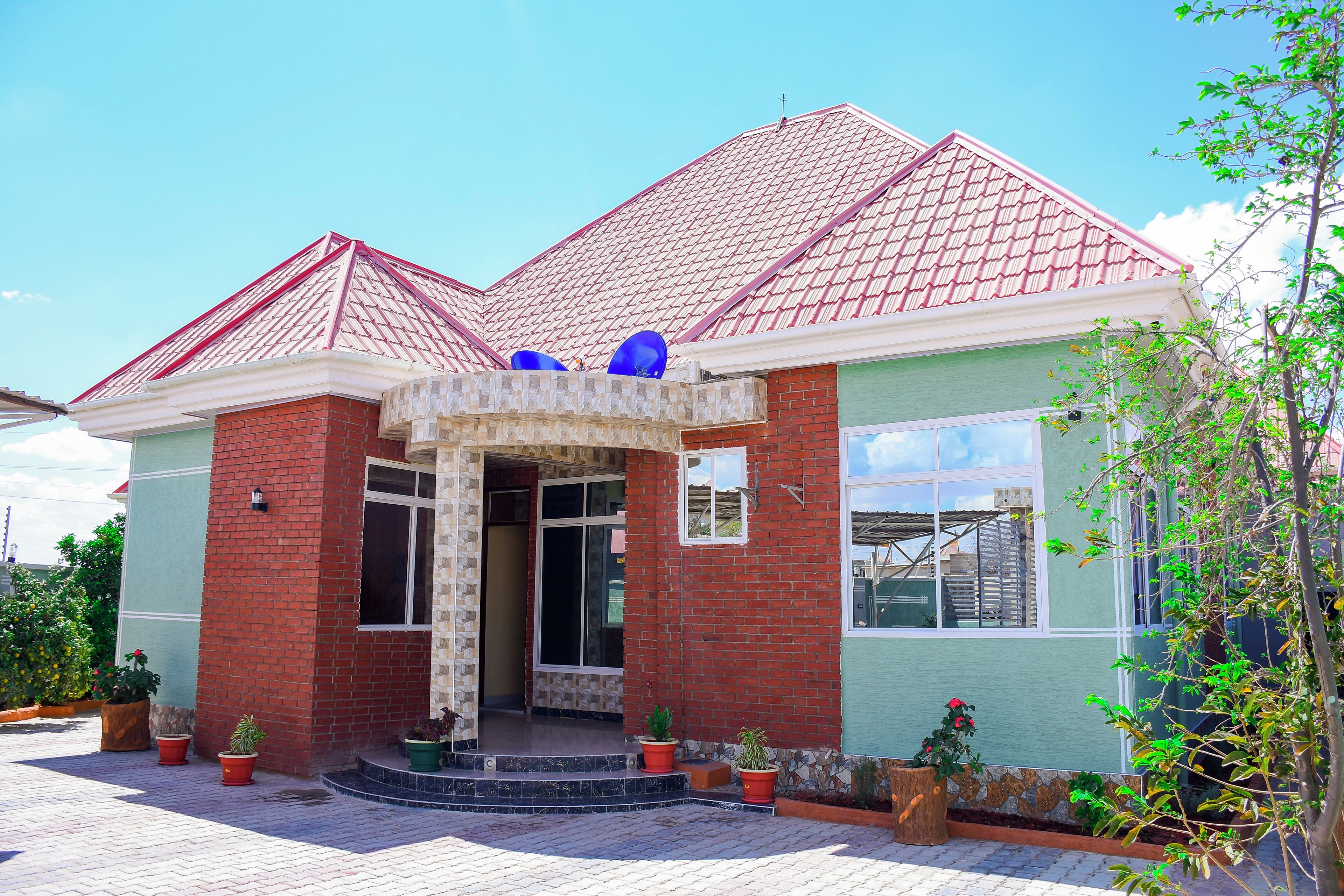 Uma casa de dois andares com telhado de telhas vermelhas, fachada de tijolos e uma pequena varanda com vasos de plantas.