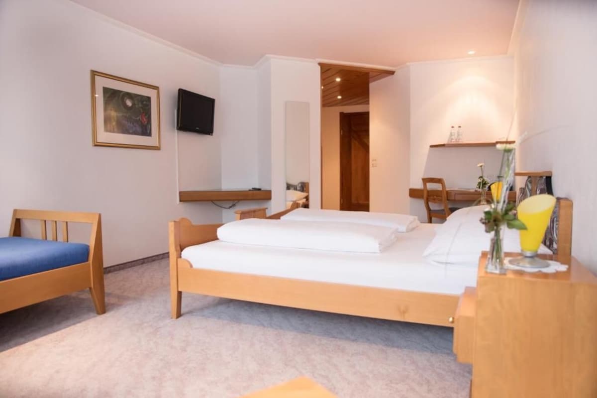 Quarto com cama, cadeira, escrivaninha e televisão.