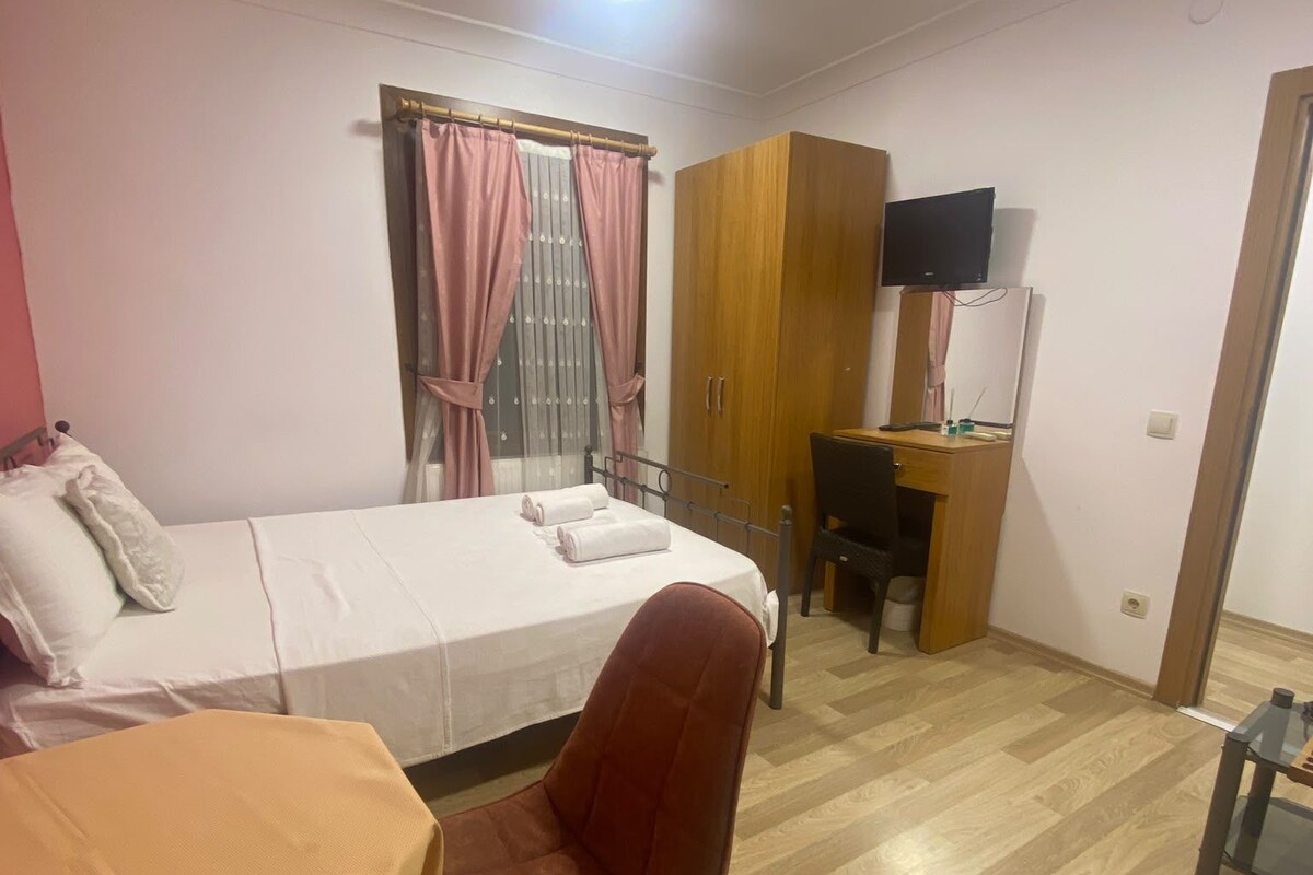 Quarto de hotel com cama, escrivaninha, cadeira, guarda-roupa e televisão.
