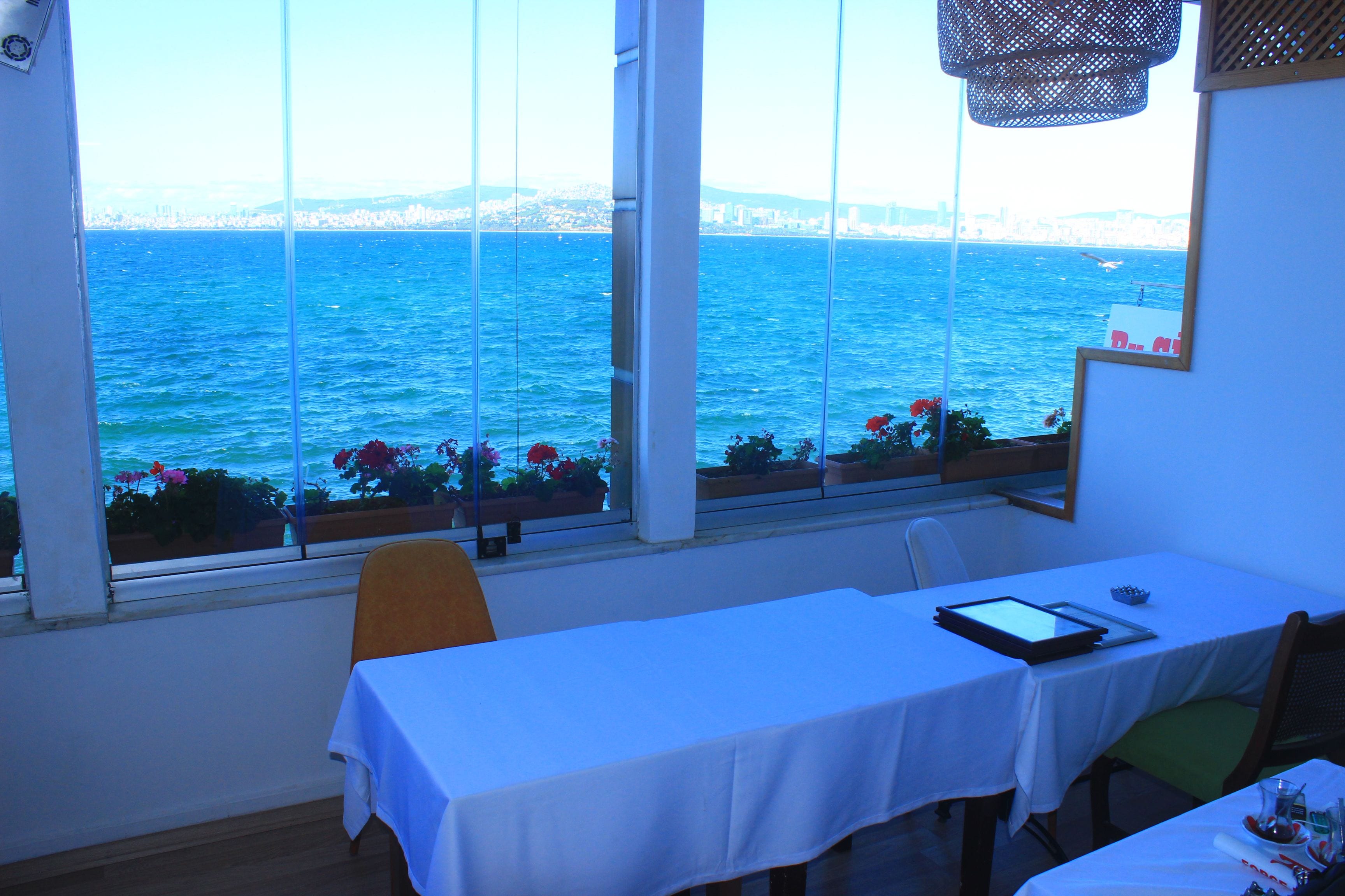 Quarto com mesa e cadeiras, vista para o mar e janela com vista da cidade.