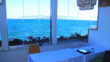 Quarto com mesa e cadeiras, vista para o mar e janela com vista da cidade.