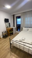 Quarto de hotel com cama, escrivaninha, cadeira, pequeno frigorífico, televisão e varanda com vista.