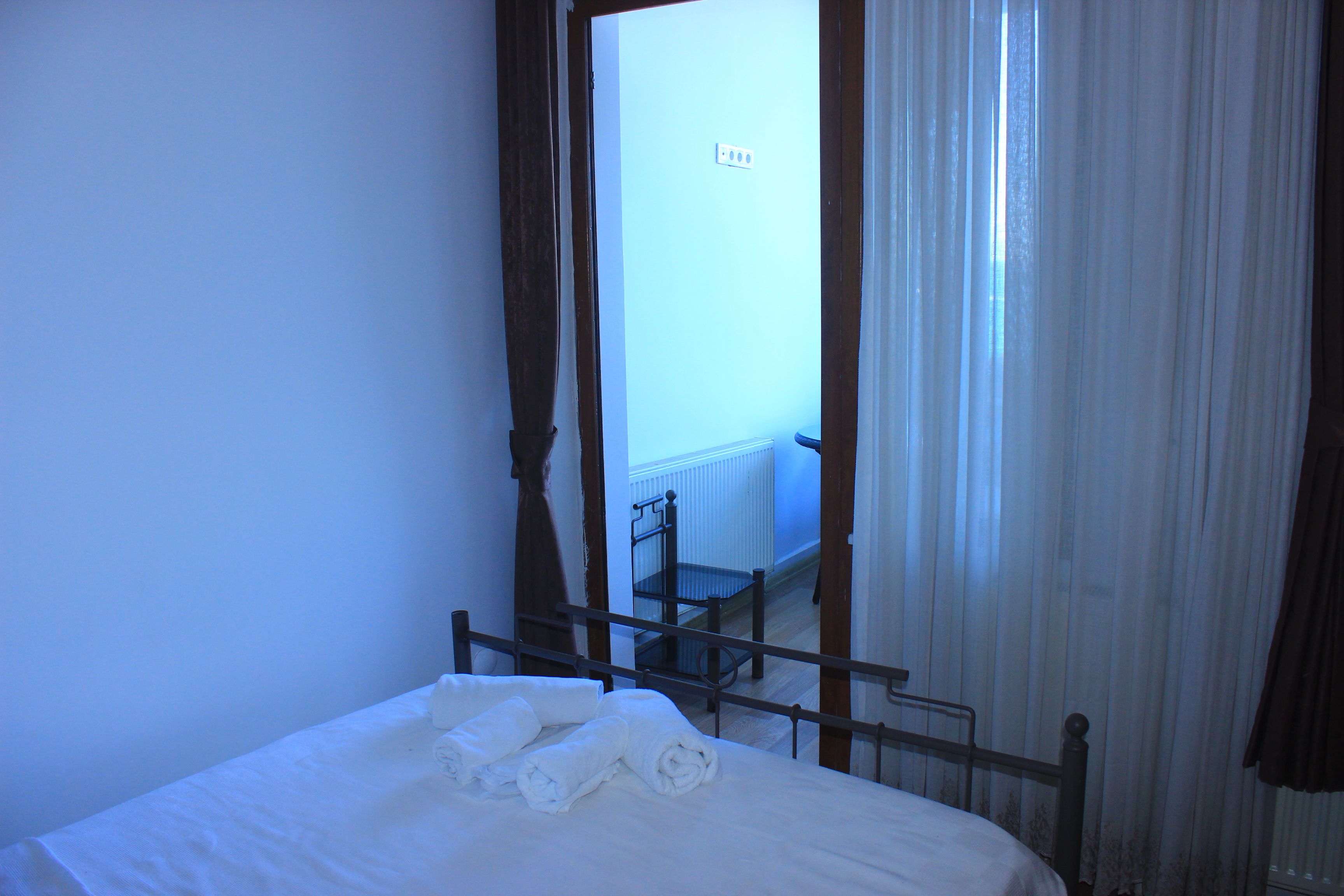 Quarto com cama, janela com cortinas e vista para uma varanda.