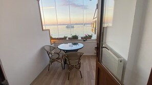 Varanda com mesa e cadeiras, com vista para um corpo de água e um horizonte urbano distante.