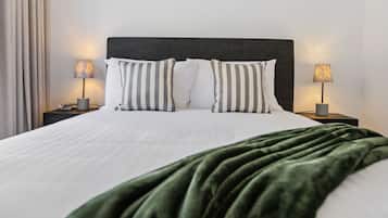 Uma cama bem arrumada com almofadas listradas, cabeceira escura e manta verde.