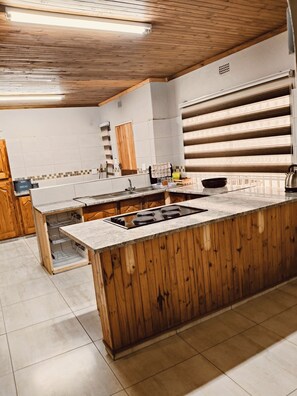 Cozinha com ilha de madeira, painel de azulejos brancos e uma grande janela com persianas.