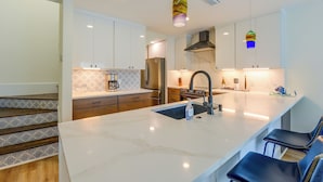 Cozinha moderna com armários brancos, bancada de mármore, forno embutido e geladeira de aço inoxidável.