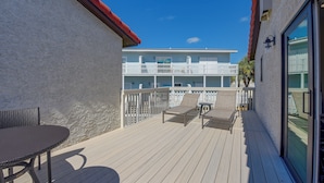 Um deck de madeira com duas cadeiras e uma mesa, com vista para um edifício de fachada branca e varandas.