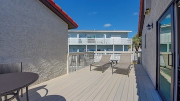 Um deck de madeira com duas cadeiras e uma mesa, com vista para um edifício de fachada branca e varandas.