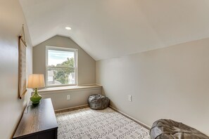 Quarto com teto inclinado, janela com vista, luminária, tapete estampado e um banquinho de couro.