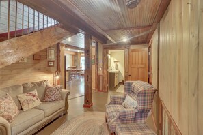 Interior acolhedor com escada de madeira, um sofá, uma poltrona xadrez e um espaço de refeições.
