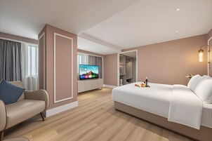 Quarto de hotel moderno com cama, área de estar, televisão e espelho.