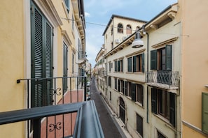 Rua estreita ladeada por edifícios com varandas e persianas.