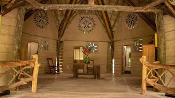Um interior rústico com piso de madeira, uma mesa central com cadeiras e arte decorativa nas paredes.