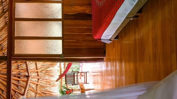 Quarto com cama, janela com vidro jateado e piso de madeira.