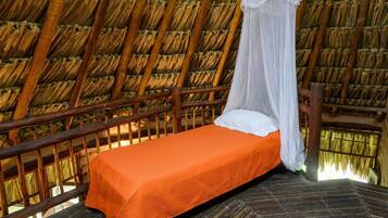 Uma cama de solteiro com colcha laranja e almofadas brancas, sob uma estrutura de telhado de palha.