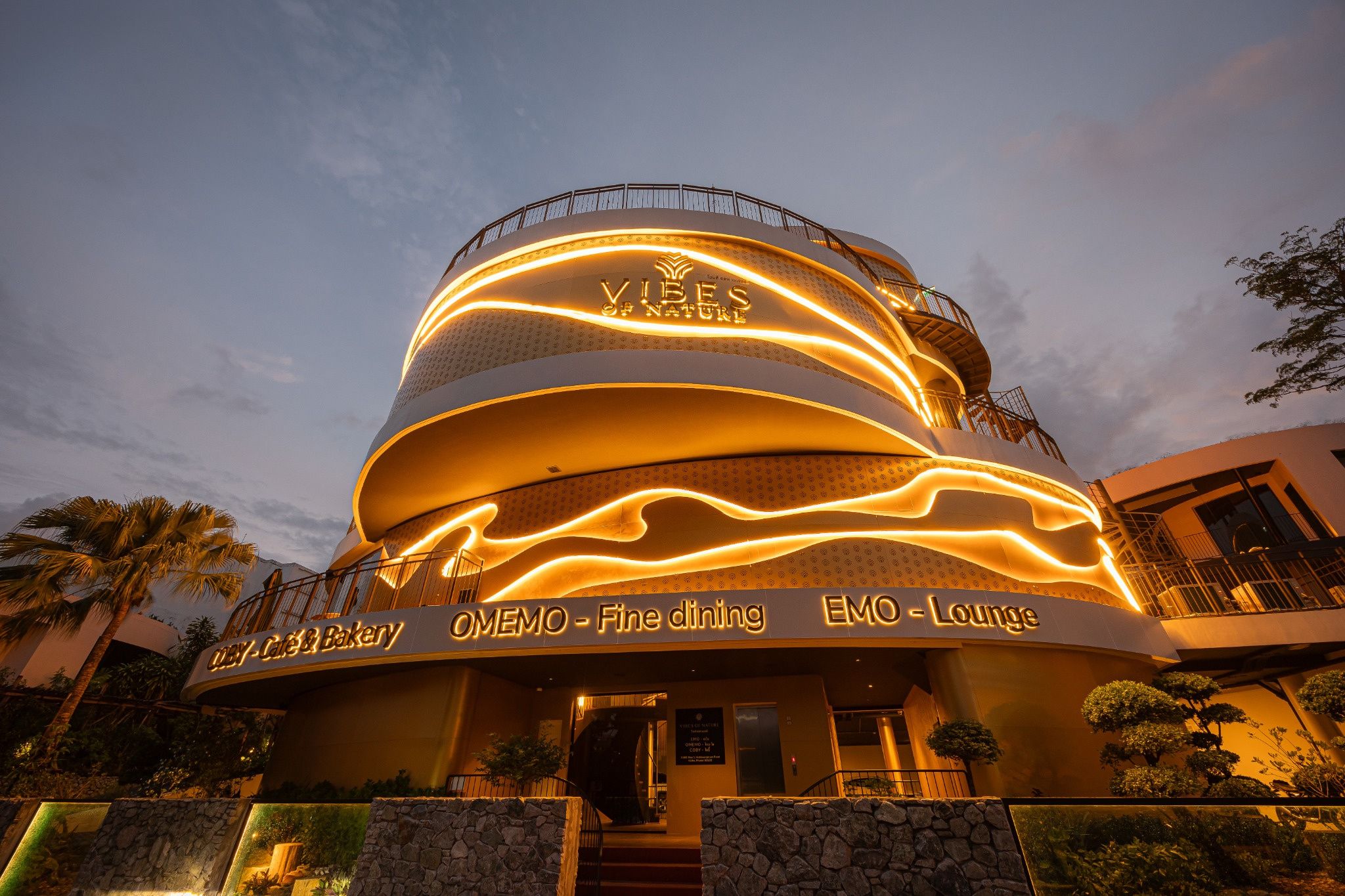 Um edifício com fachada curva, com a inscrição 'EMO - Fine dining' e 'EMO - Lounge', e um letreiro que diz 'VIBES OF NATURE'.