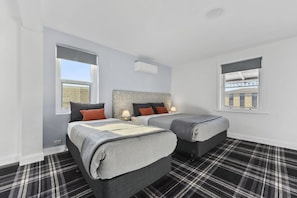 Quarto com duas camas, cabeceira, janela e piso quadriculado em preto e branco.