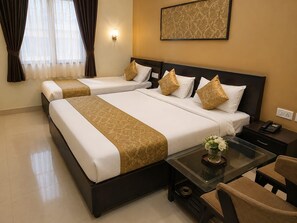 Quarto de hotel com duas camas, uma mesinha de cabeceira com telefone, uma pequena mesa com um vaso e uma cadeira.
