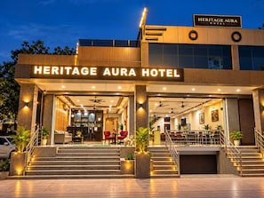 Exterior do Heritage Aura Hotel, com design moderno, destacando uma entrada imponente, uma área de recepção e uma escadaria que leva ao lobby.