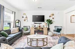 Uma sala de estar moderna com um sofá cinzento, duas poltronas, uma mesa de centro e uma TV de tela plana na parede.