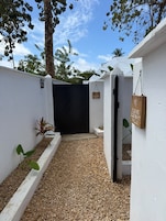 Uma entrada fechada com um caminho de cascalho que leva a um edifício, cercado por muros brancos e árvores.