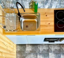 Cozinha com pia de aço inoxidável, escorredor de louça, recipiente verde e micro-ondas embutido.