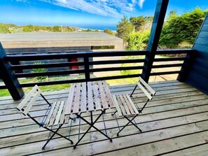 Um deck de madeira com mesa e cadeiras, com vista para o oceano e vegetação.