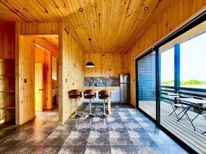 Interior em madeira com cozinha, área de bar e grandes portas de vidro deslizantes que dão para um deck externo.