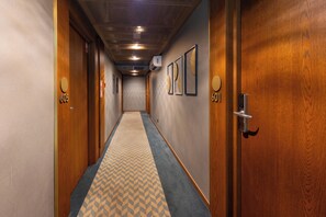 Corredor de hotel com portas de madeira, placas de número nas portas e carpete estampado.