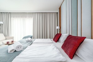 Quarto de hotel com duas camas, um sofá, uma poltrona e uma janela com cortinas.