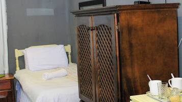 Quarto de hotel com cama, guarda-roupa, televisão na parede e uma pequena mesa com chaleira e chávenas.