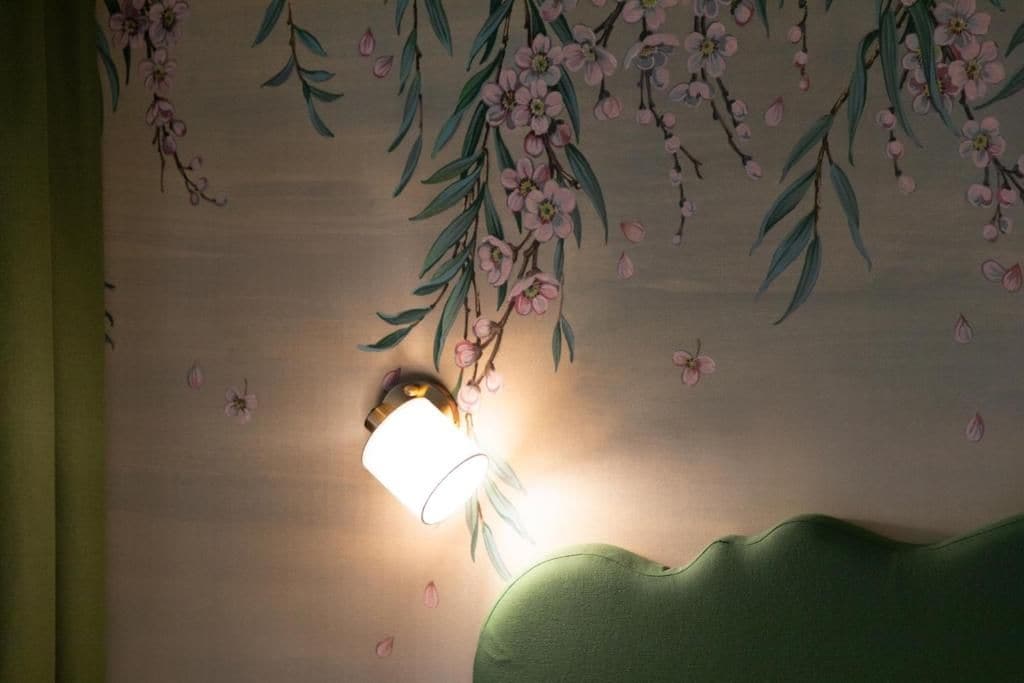 Quarto com papel de parede floral e luminária pendente.